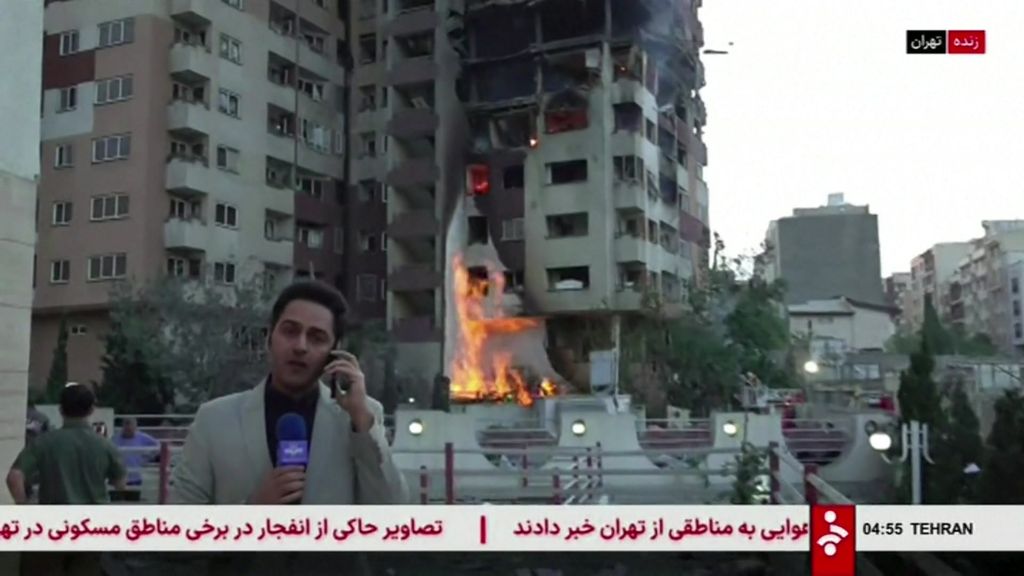 Iranian journalist speaks in front of burning building after Israel ...