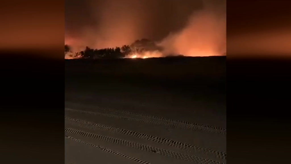 A fire burns at night near the Teewah Beach township. - ABC News